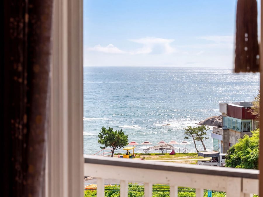 Vista do mar a partir de uma varanda com guarda-corpo, um edifício com design moderno e área de estar ao ar livre com guarda-sóis.