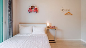 Quarto com cama, travesseiros, mesa de cabeceira, abajur, suporte para chaves e um modelo de carro decorativo.
