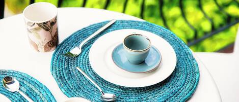 Mesa posta com um jogo de mesa azul tecido, um prato branco, uma xícara azul e uma colher de prata.