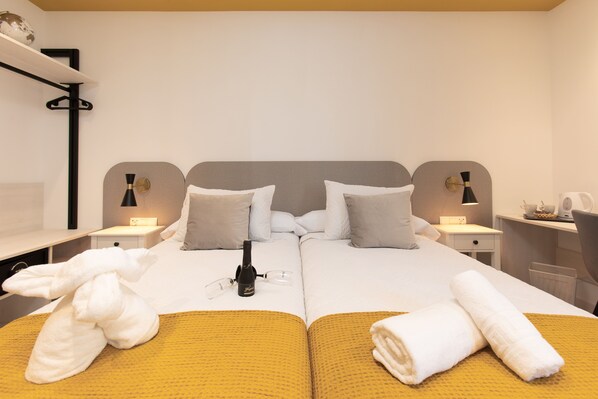 Cama de casal com duas almofadas, mesa de cabeceira com abajur e uma garrafa de champanhe.