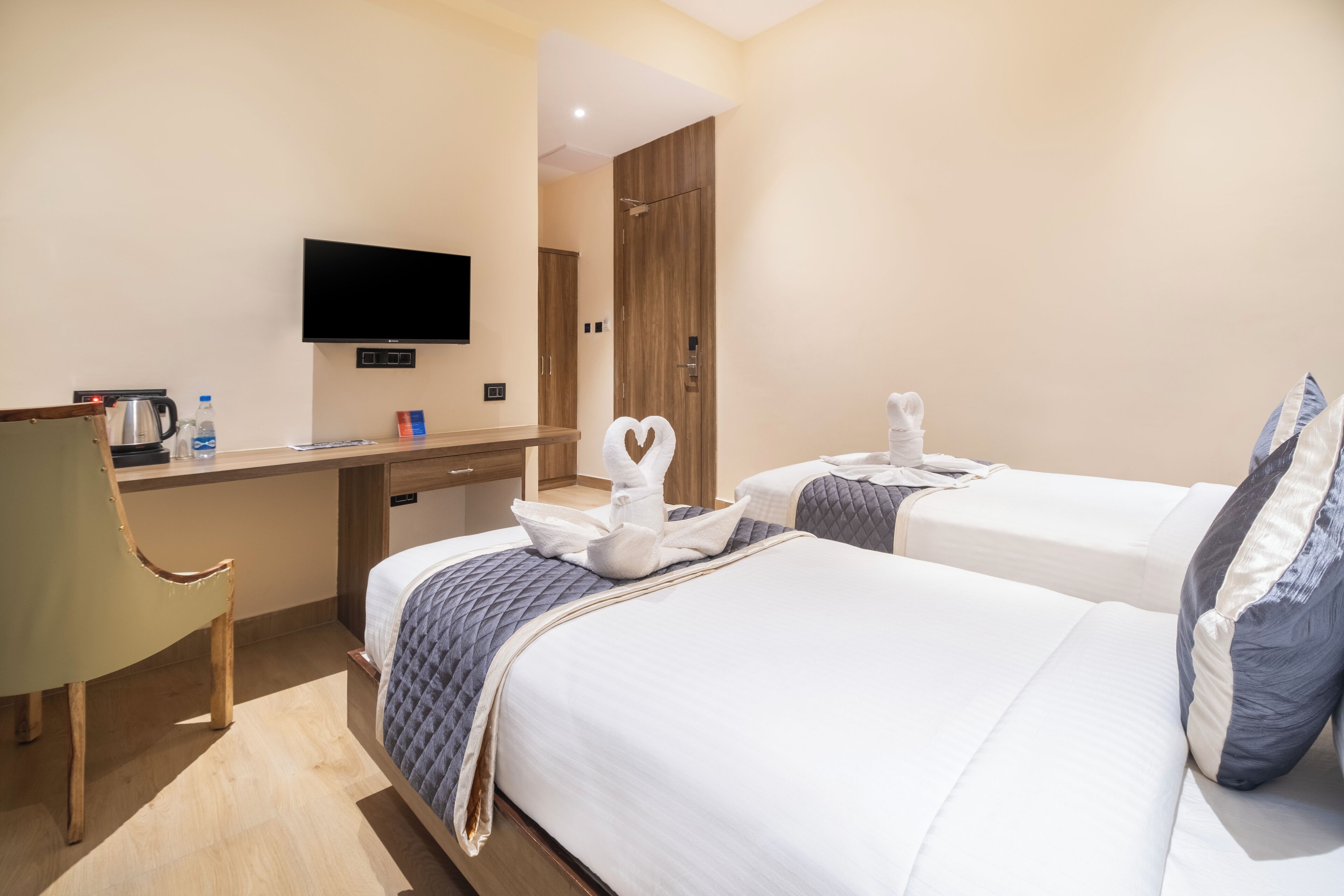 Quarto de hotel com duas camas, uma escrivaninha, uma cadeira, uma televisão e área de chuveiro.