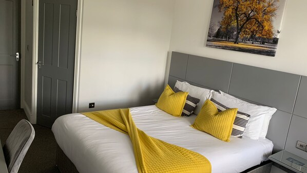 Quarto de hotel com uma cama, cabeceira cinzenta e um quadro de folhas de outono na parede.