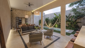 Ampla sala de estar com parede de pedra, rede e vista para um jardim.
