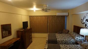 Quarto com cama, escrivaninha, televisão, guarda-roupa e ventoinha no teto.