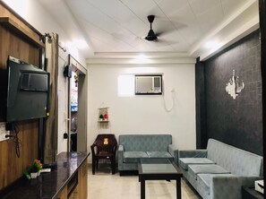 Uma sala de estar com sofá, mesa de centro, televisão e aparelho de ar condicionado.