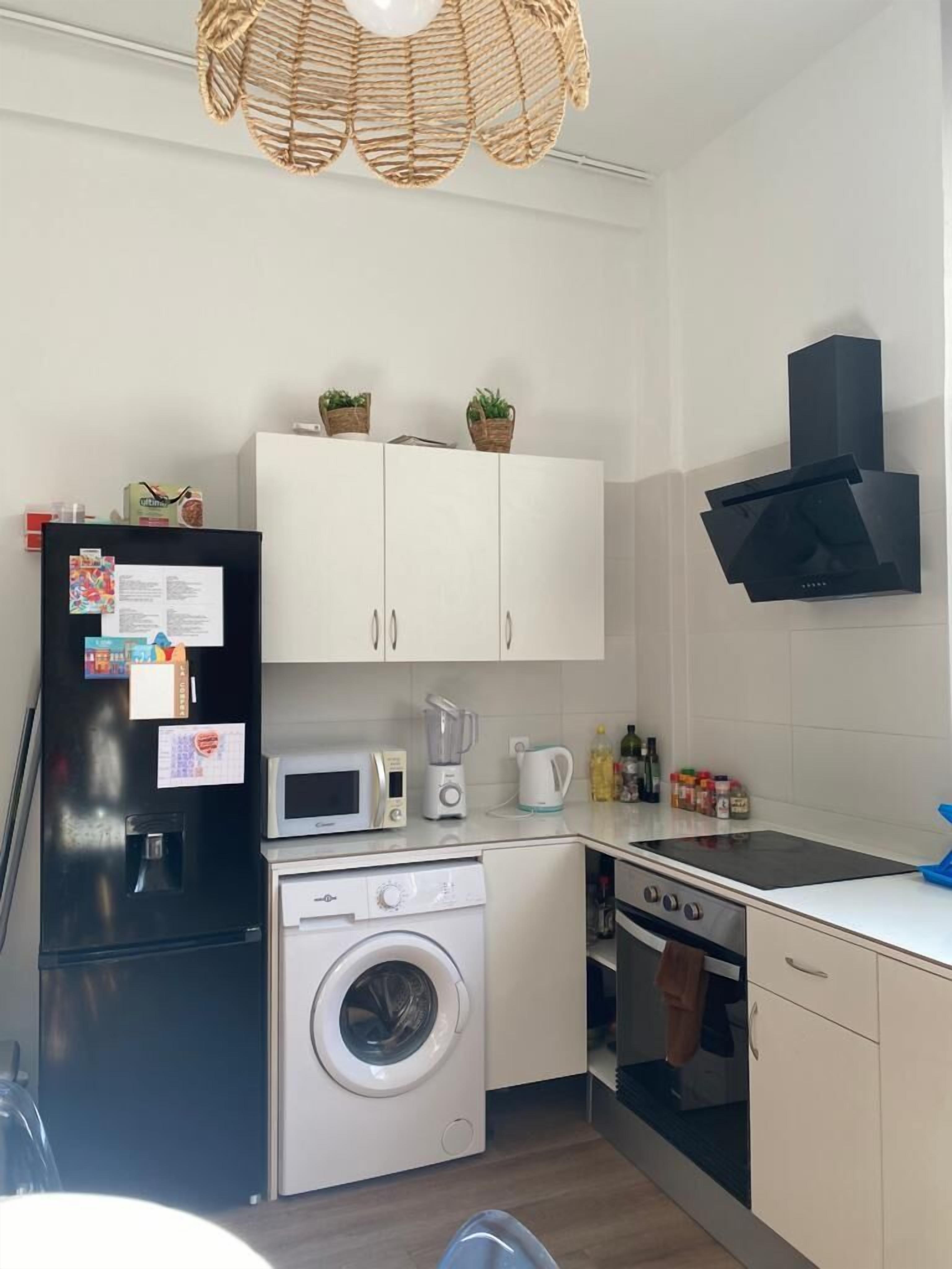 Uma cozinha compacta com máquina de lavar, micro-ondas e coifa preta.