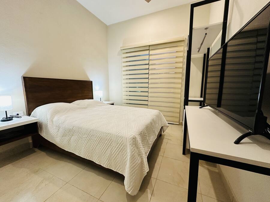 Quarto com cama, mesa de cabeceira, abajur e um espelho grande.