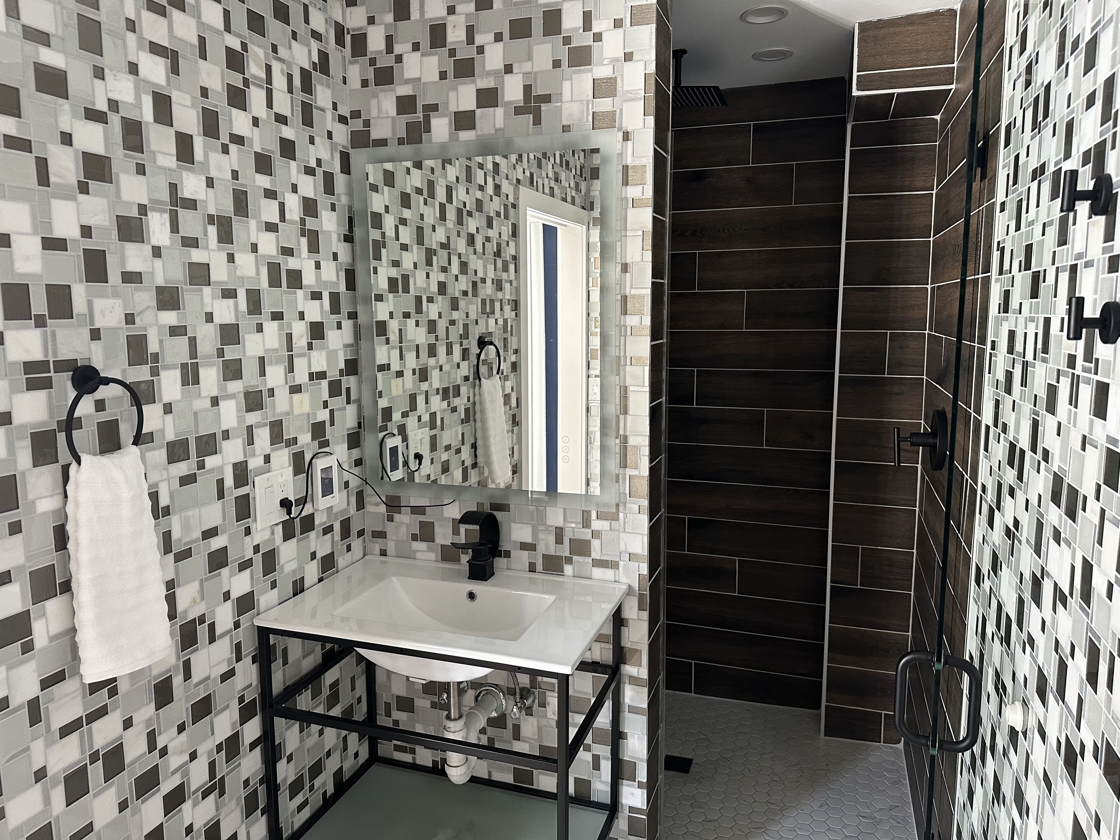 Um banheiro moderno com mosaico de azulejos na parede, pia branca e espelho.