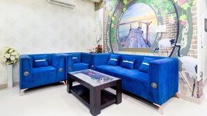 Um sofá modular azul com uma mesa de centro de vidro em um quarto com parede de tijolos e um mural de um pôr do sol sobre uma ponte.
