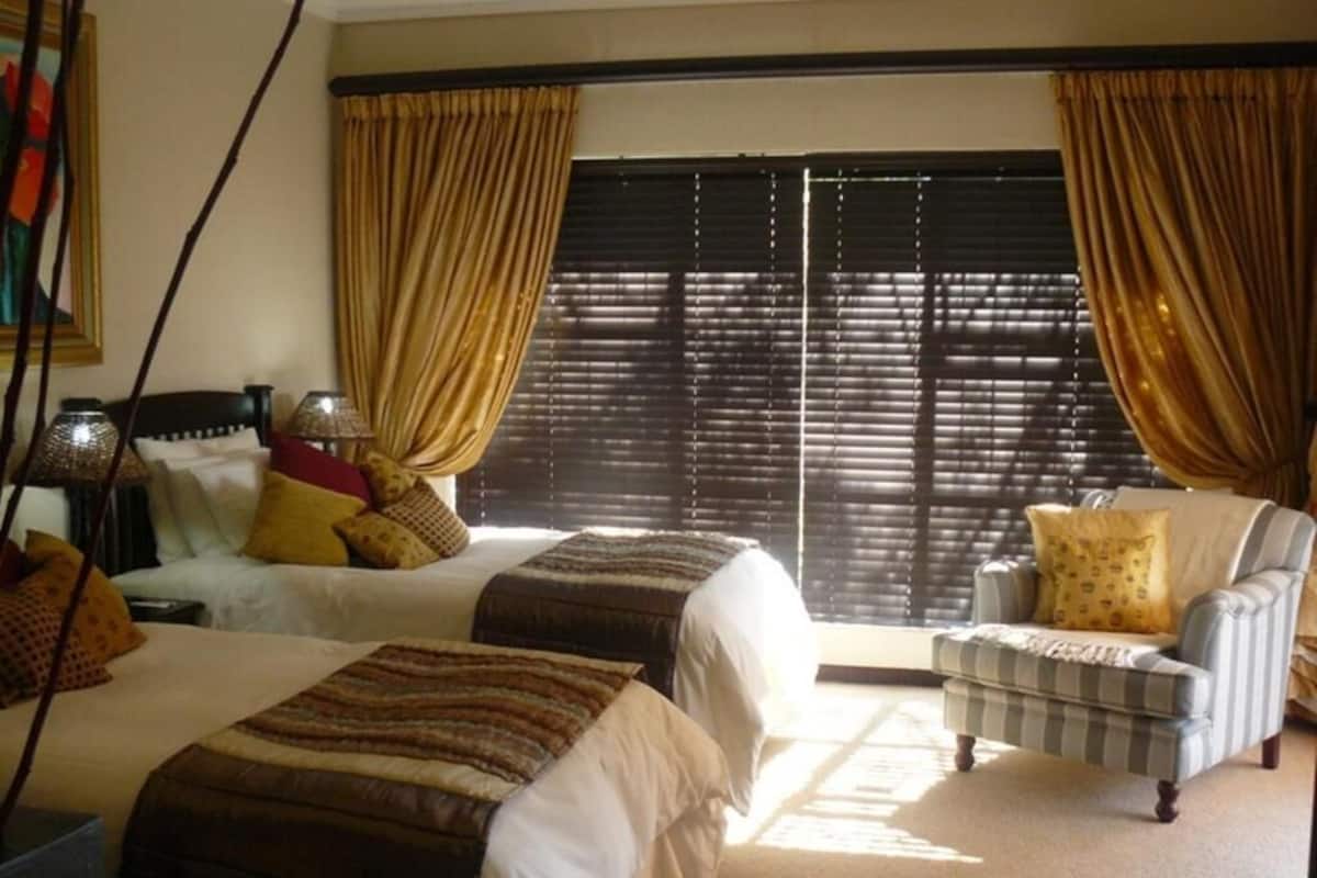 Quarto de hotel com duas camas, uma cadeira e uma janela grande com cortinas.
