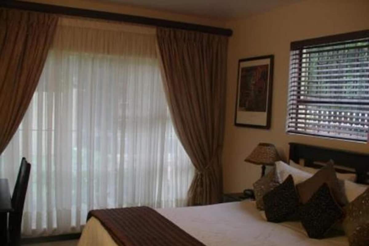 Quarto de hotel com cama, cortinas, abajur, um quadro na parede e janela com persianas.