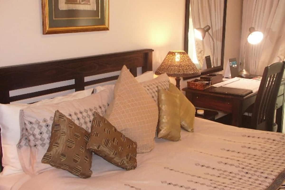 Quarto de hotel com cama, almofadas, escrivaninha com luminária e espelho.