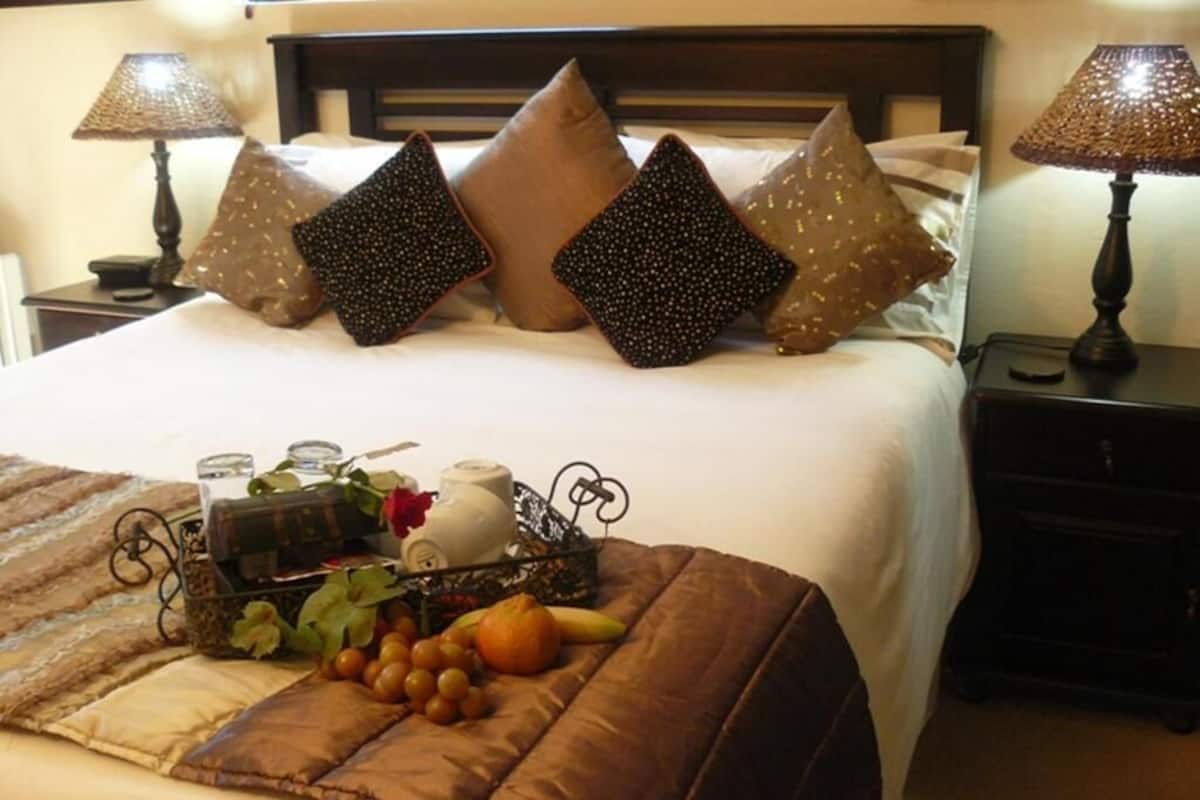 Cama bem arrumada com travesseiro marrom, bandeja com frutas e um vaso, e duas luminárias em mesas de cabeceira.
