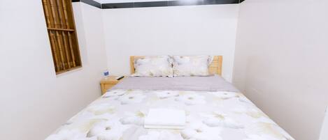 Uma cama bem arrumada com colcha florida, uma cabeceira de madeira e uma mesa de cabeceira com abajur.