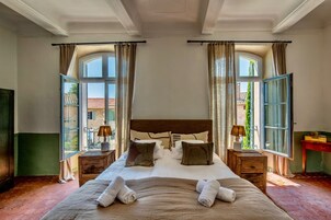 Um quarto espaçoso com uma cama grande, duas mesas de cabeceira e vista pelas janelas abertas.
