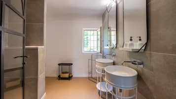 Uma casa de banho moderna com cabine de duche em vidro, um espelho grande e duas pias.
