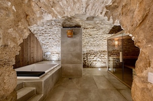 Um quarto de spa com parede de pedra, parede de ripas de madeira, uma banheira e box de vidro.