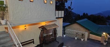 Uma área de estar moderna ao ar livre, com escadas, uma cadeira balanço e vista para uma cordilheira.