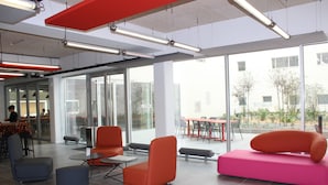 Um espaço interior moderno com assentos laranja e rosa, janelas amplas e vista para o exterior.