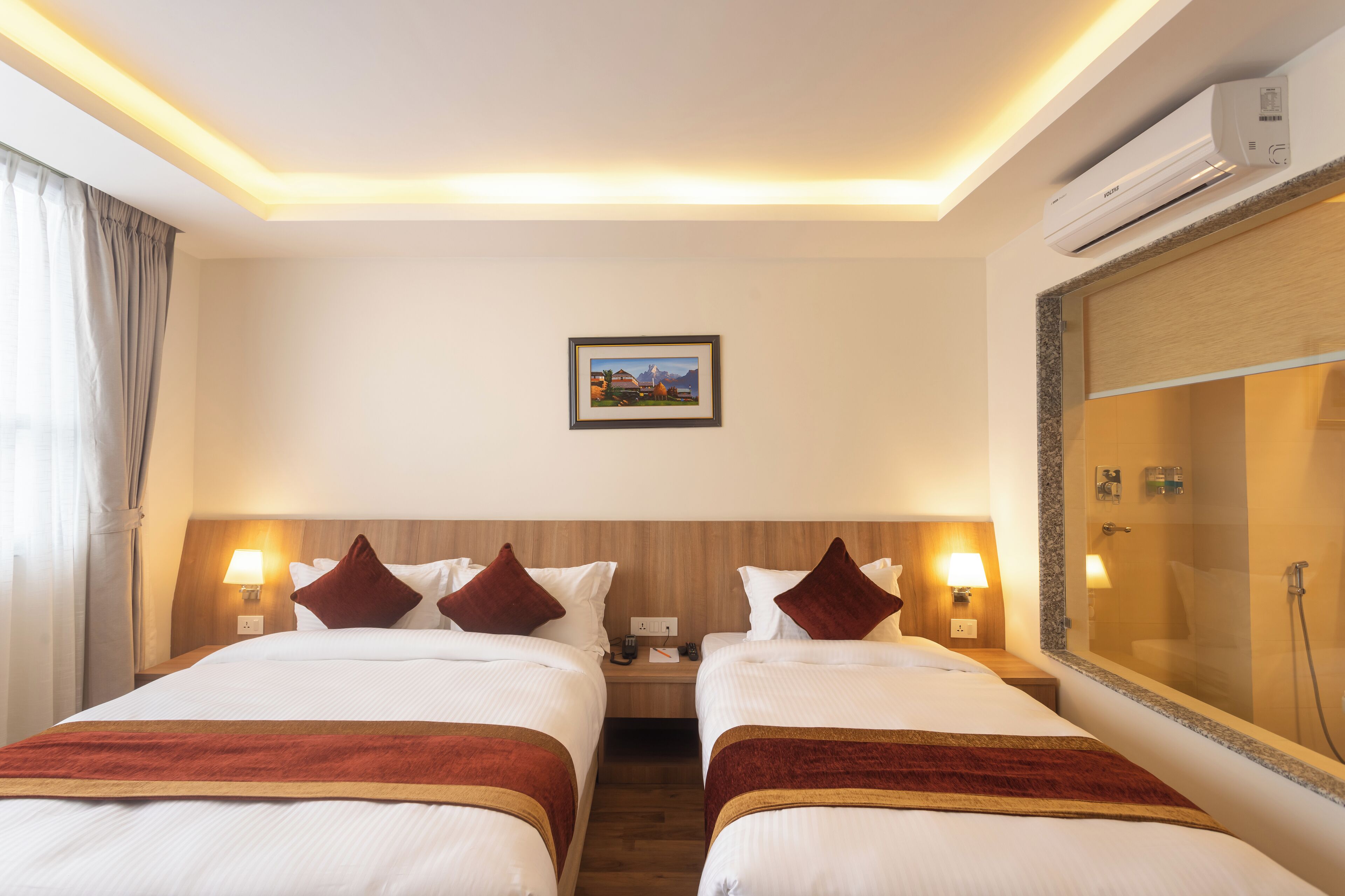 Quarto de hotel com duas camas, um espelho grande, um ar condicionado e um quadro na parede.