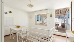 Uma sala clara e luminosa, com uma mesa de jantar, cadeiras, um banco branco e uma janela, oferecendo vista para o exterior.