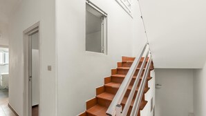 Uma escadaria com guarda-corrimão branco e degraus em terracota que levam a um patamar.
