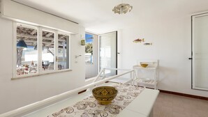 Um quarto com uma mesa de jantar, uma tigela decorativa, uma cadeira branca, uma estante branca com uma tigela e uma janela com vista para o exterior.