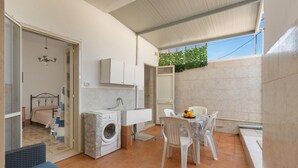 Um espaço compacto com máquina de lavar roupa, área de refeições com cadeiras e mesa, cama e pequena cozinha.