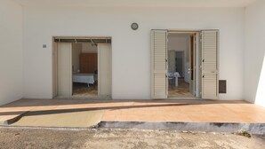 Um edifício branco com duas portas abertas que dão acesso a espaços interiores, um pátio com azulejos e uma pequena área externa.