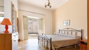 Quarto com cama, cómoda de madeira, luminária e porta de acesso a um banheiro.