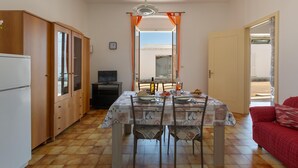 Uma sala de jantar com uma mesa posta para quatro pessoas, um armário de madeira e um sofá vermelho.