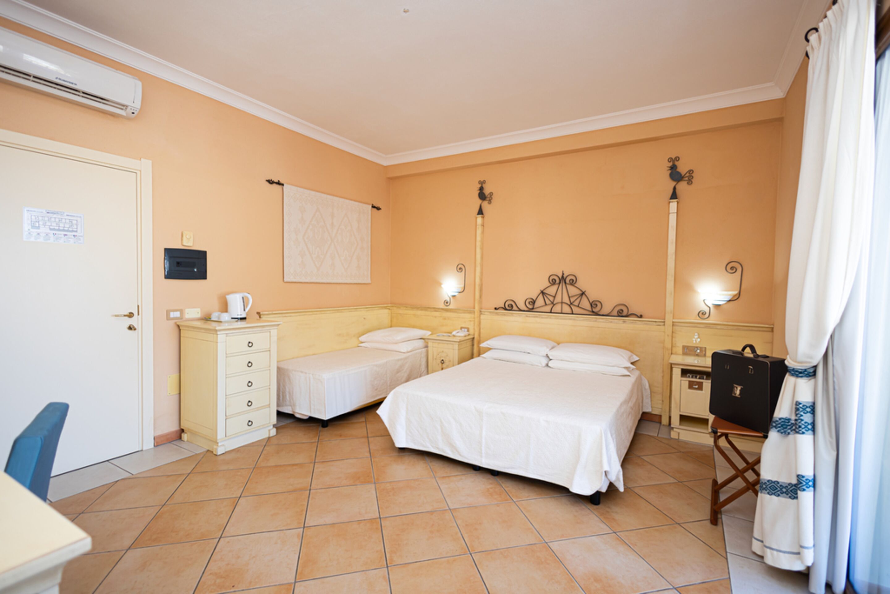 Quarto de hotel com duas camas, uma mesa, uma cadeira, um guarda-roupa e um banheiro.