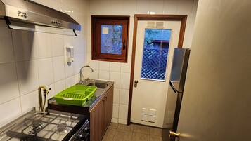 Uma cozinha compacta com fogão a gás, pia e janela com vista para uma cerca.