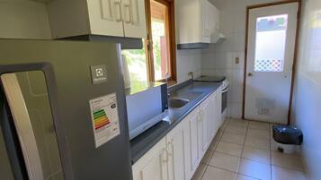 Cozinha com armários brancos, geladeira de aço inoxidável, uma janela e uma porta com janela.