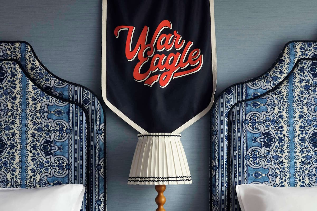 Quarto de hotel com duas camas, uma mesa de cabeceira com abajur e um banner decorativo.