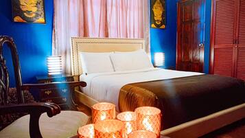 Quarto com cama, mesa de cabeceira, cadeira e objetos decorativos.