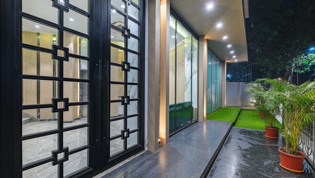 Entrada de um edifício moderno com porta de vidro, caminho pavimentado e plantas em vasos.