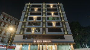 Um hotel de vários andares chamado Eden Serenity, com fachada moderna, janelas iluminadas e entrada visível.