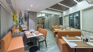 Um restaurante moderno com boxes e mesas, parede estampada e teto com iluminação linear.