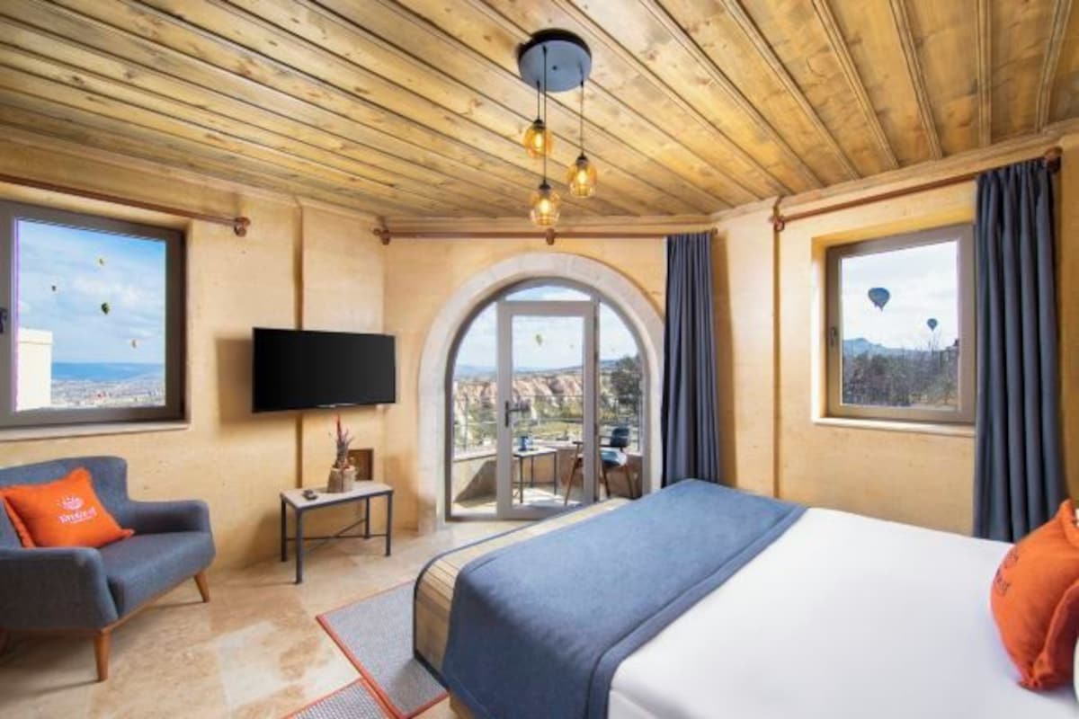 Quarto com cama, televisão, sofá e varanda com vista.
