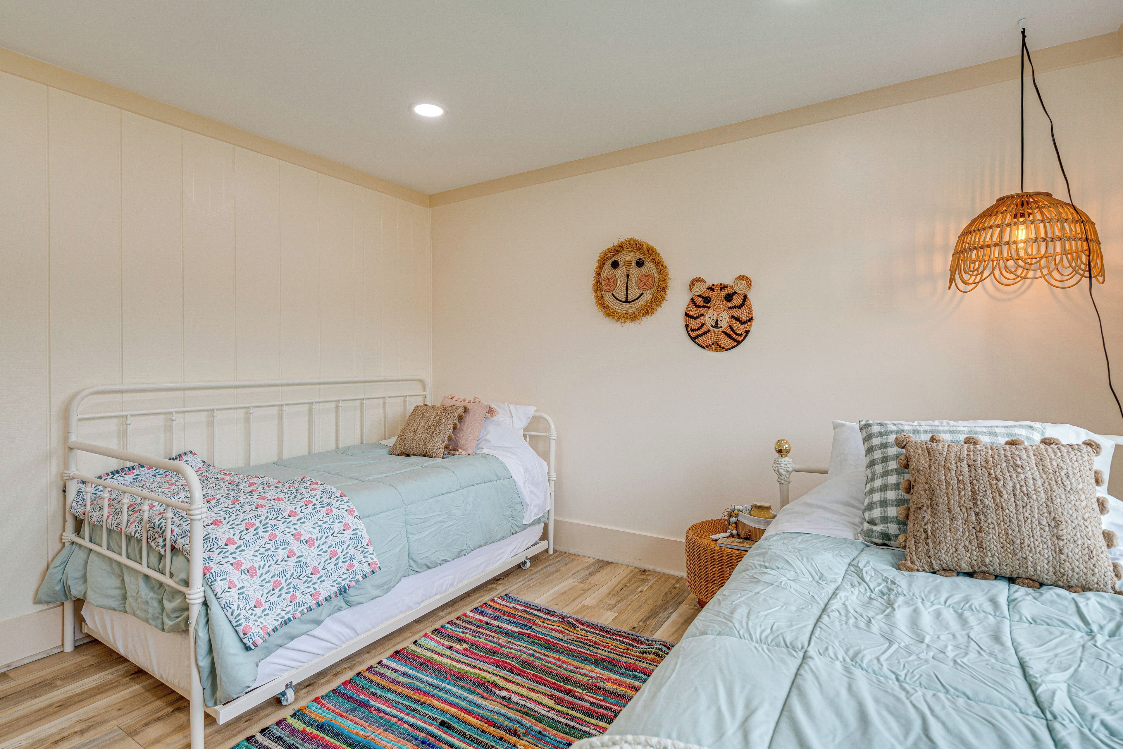 Quarto com duas camas, um tapete colorido, um candeeiro fixado na parede e duas obras de arte decorativas.