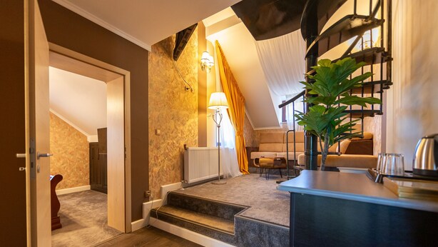 Um interior moderno com uma escada que dá para um espaço de loft, uma área de estar com sofá e poltronas, e um balcão de bar.