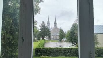 Visão pela janela de uma igreja com duas torres, um gramado verde e um banco.