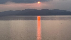 Água calma refletindo o sol, com montanhas ao fundo.