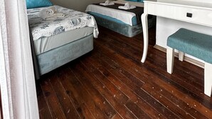 Quarto com duas camas, uma escrivaninha, um banco e uma janela com cortinas.