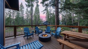 Um deck com cadeiras Adirondack azuis, um braseiro e uma mesa de madeira.