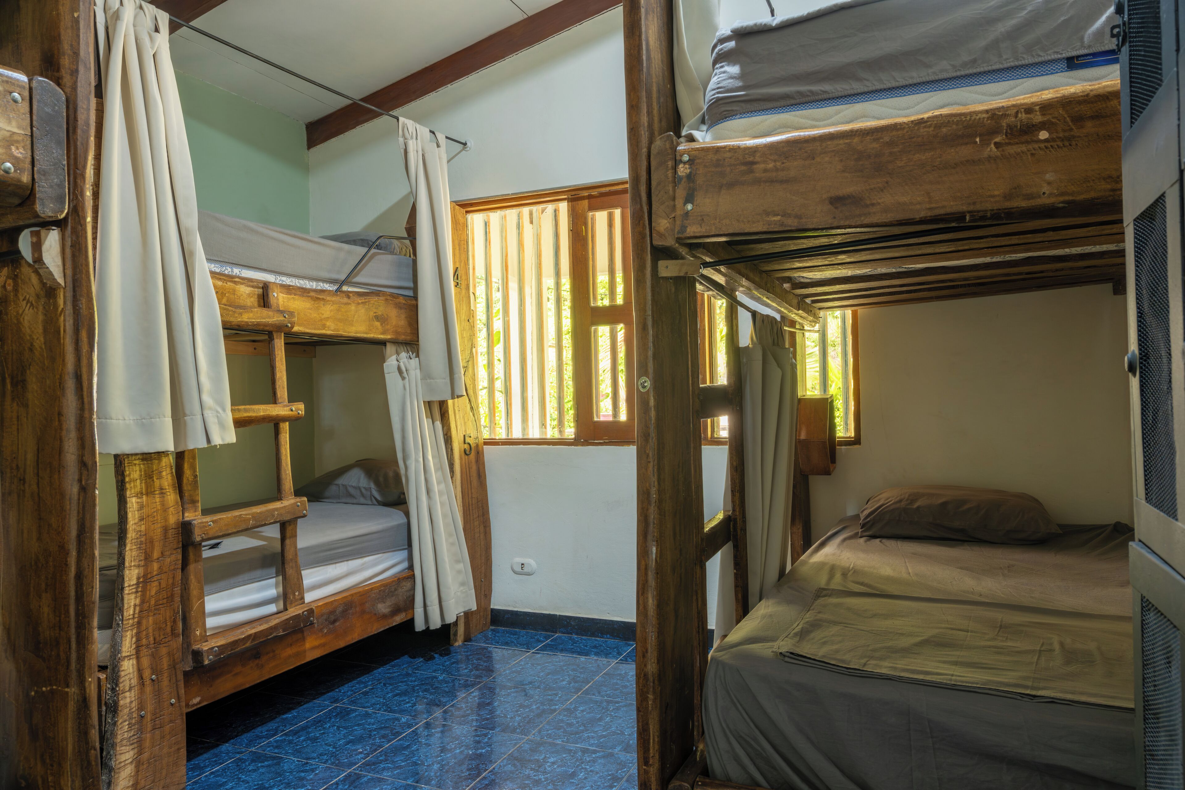 Quarto com beliches, paredes de madeira e uma janela com persianas verticais.