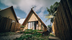 Uma cabana com telhado inclinado, cerca de madeira e um pequeno jardim com plantas e um banco.