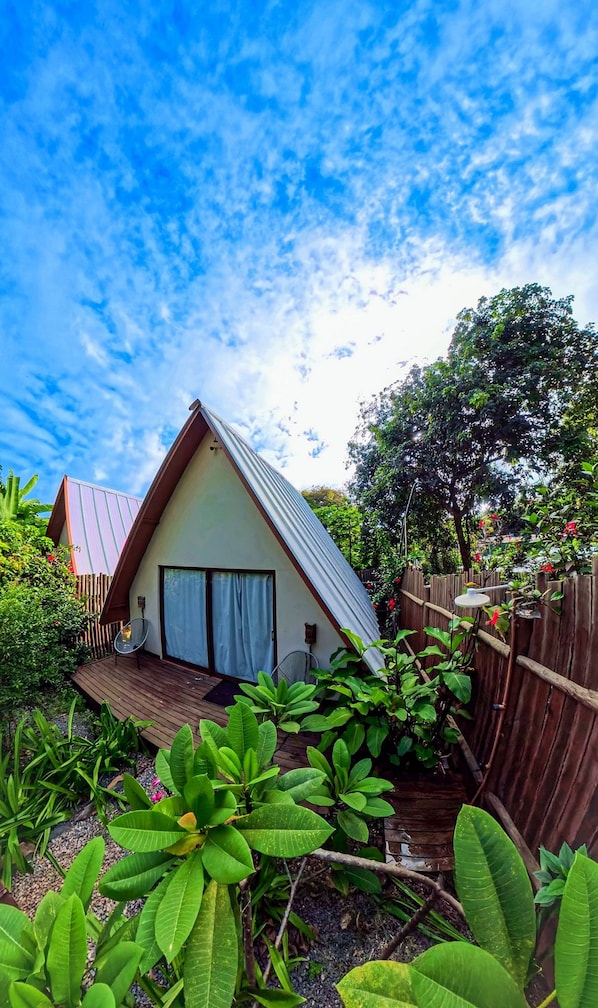 Uma casa com telhado inclinado, um deck de madeira e um jardim com diversas plantas.