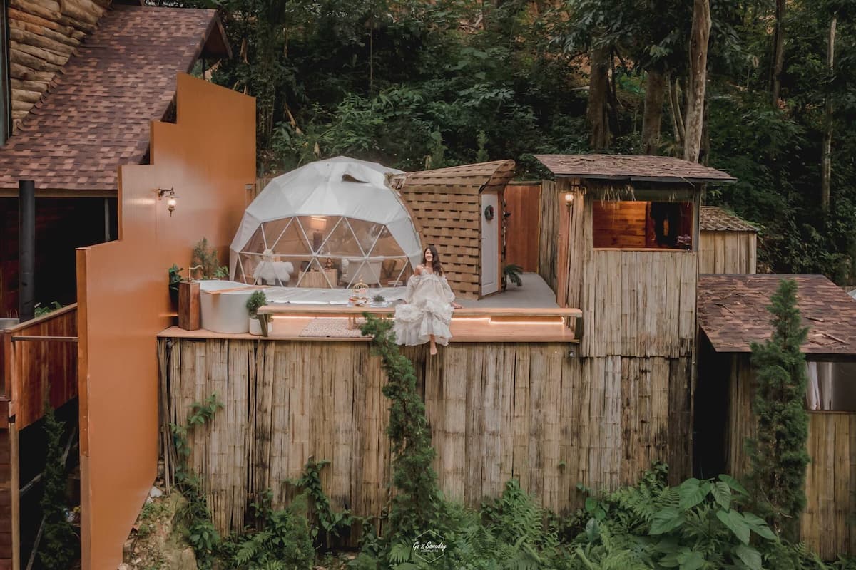 Ambiente rústico ao ar livre, com estrutura de madeira, uma tenda em forma de cúpula e um pequeno edifício de madeira.
